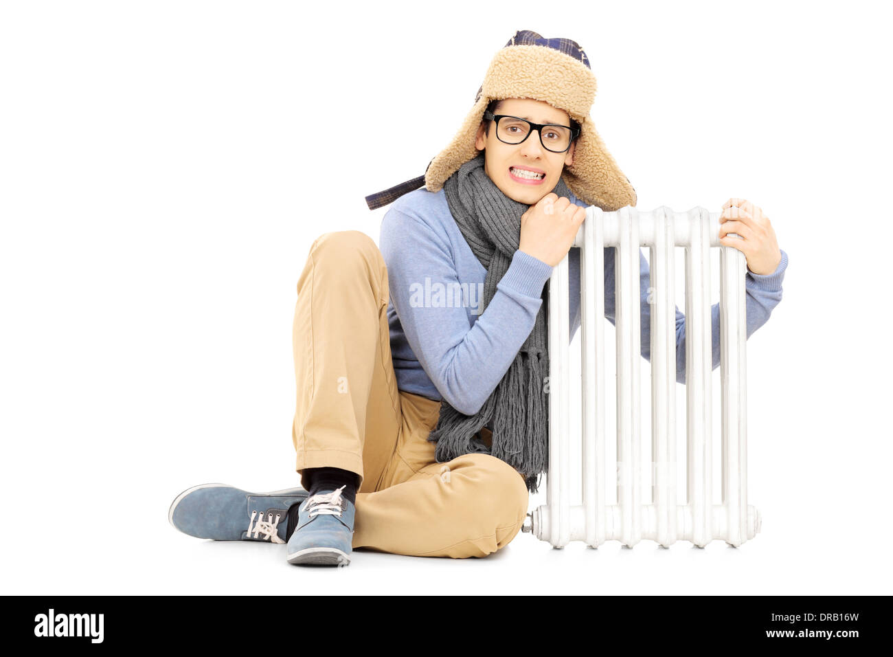Freezing young guy in winter hat and scarf sitting next to radiator ...