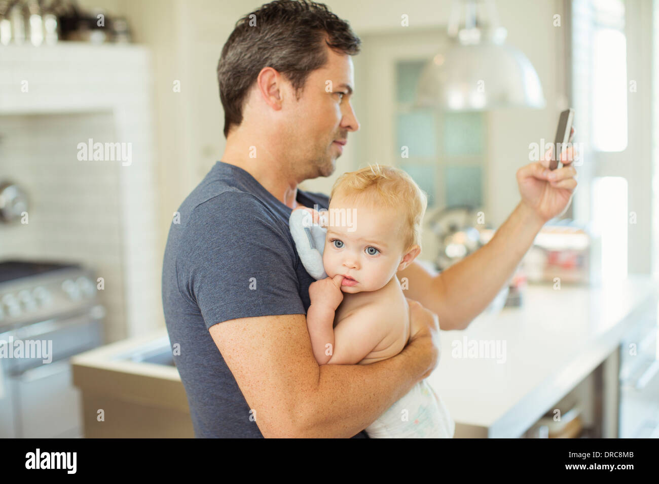 Father using cell phone and holding baby Stock Photo - Alamy
