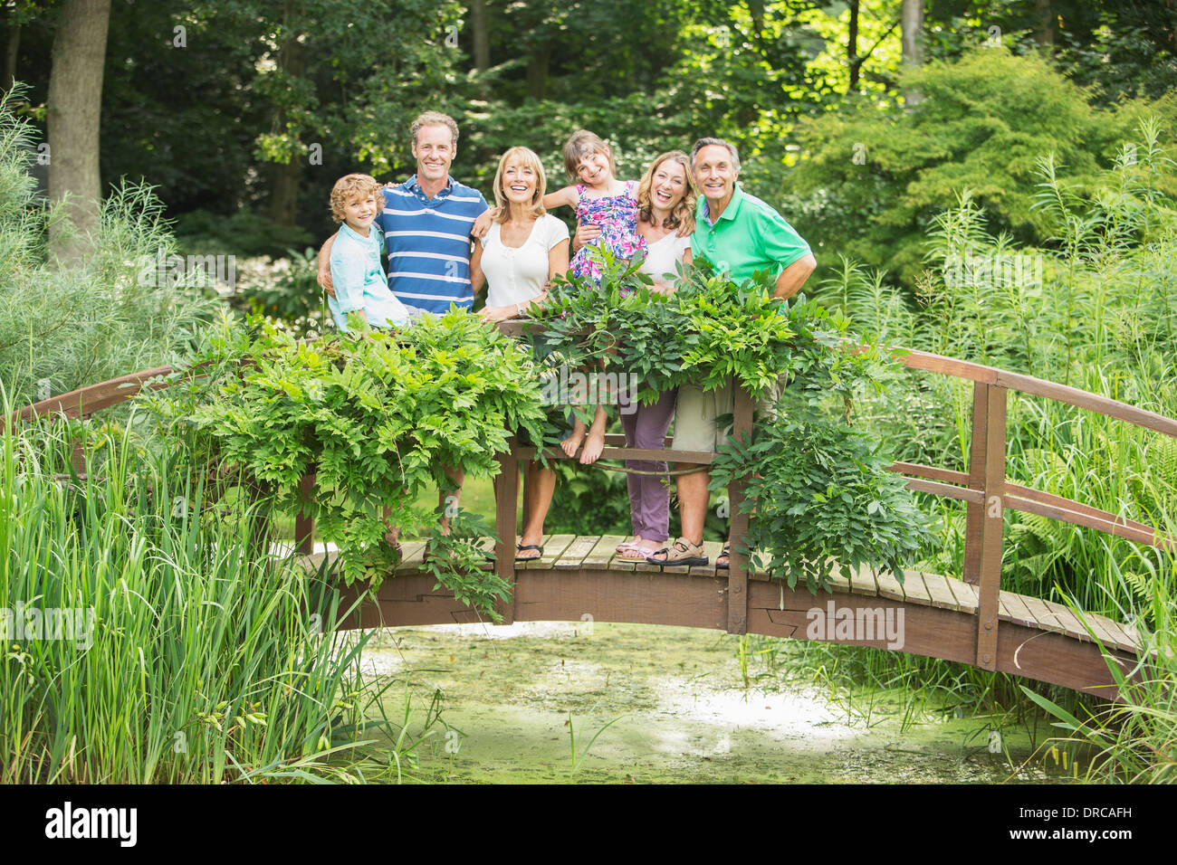 Multi-generation family standing on wooden footbridge over pond Stock ...