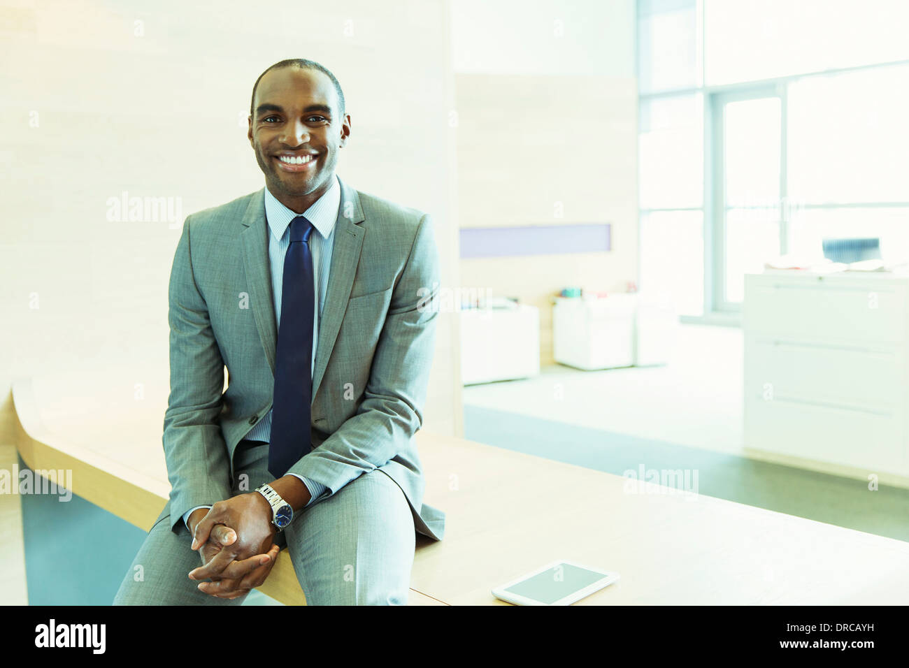 Portrait of a smiling young businessman sitting at desk in office Stock ...