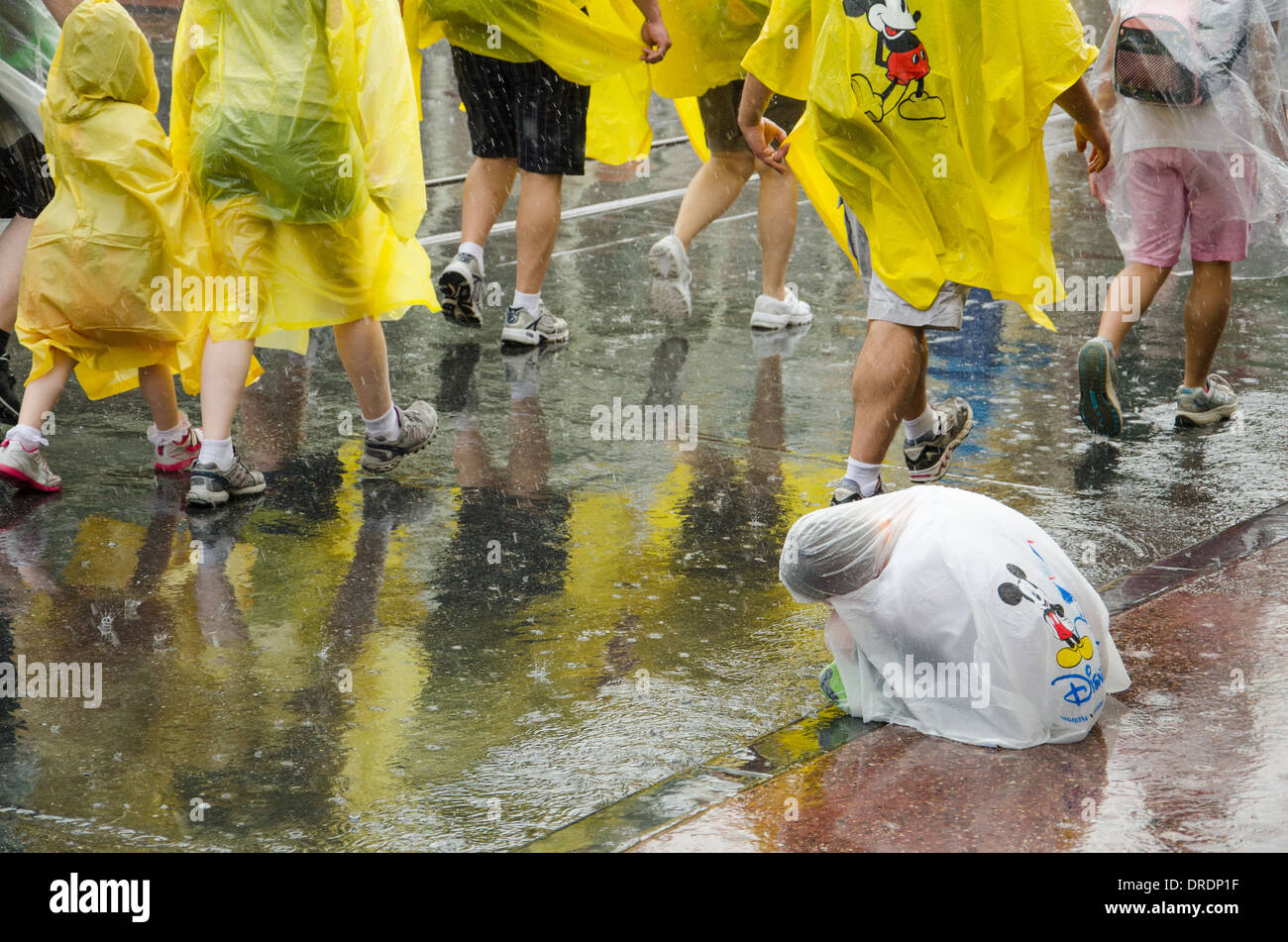 A disappointed child wrapped up in a poncho with the Magic Kingdom ...