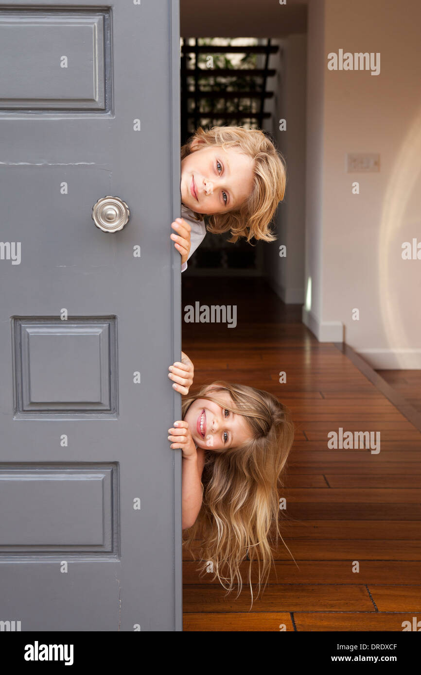 Siblings peeking out door Stock Photo - Alamy