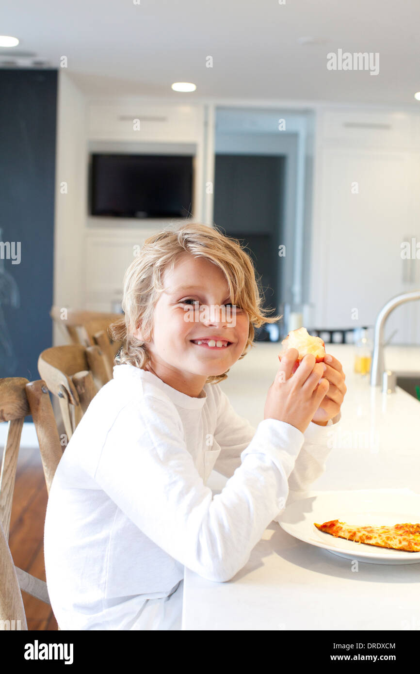 Boy sitting at kitchen counter eating pizza Stock Photo - Alamy