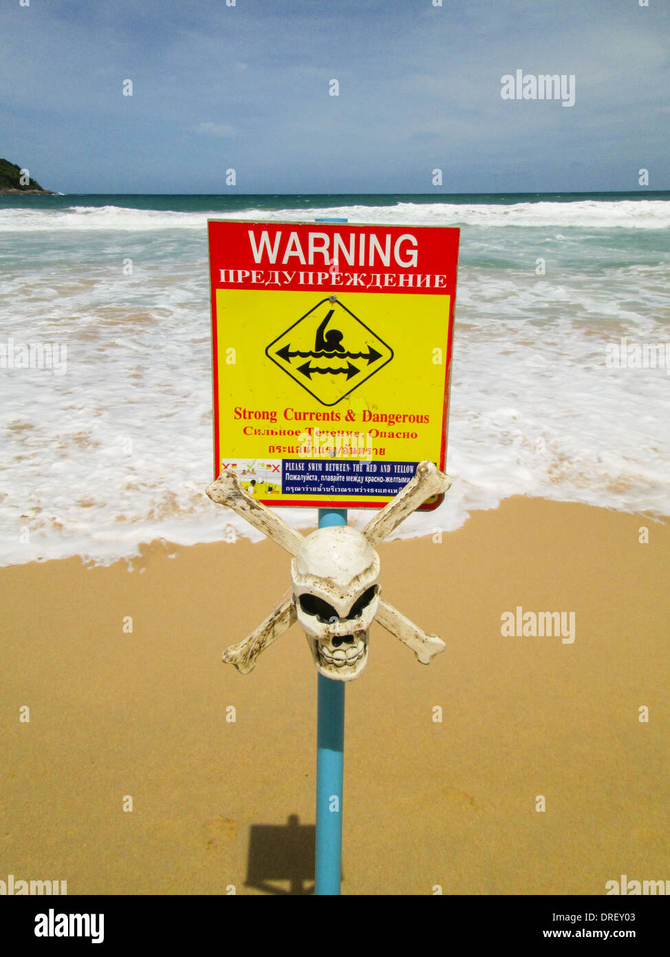 yellow sign post with skull is warning of dangerous currents on a beach ...