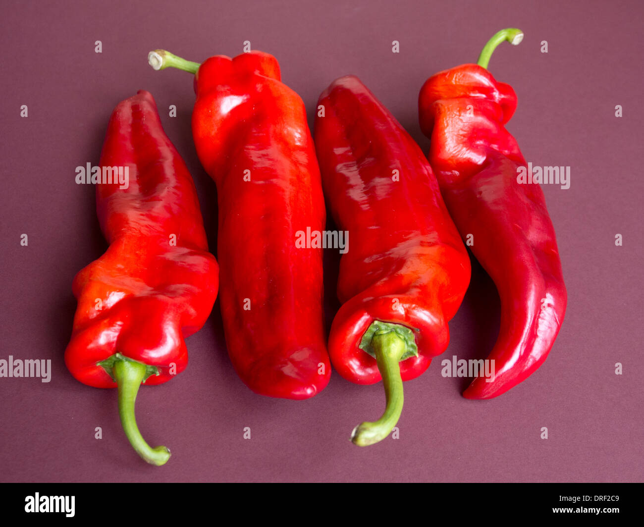 a still life of four shiny red capsicum peppers 'head-to-tail' on a ...