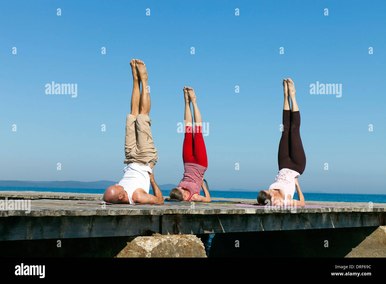 People practising yoga on boardwalk, doing shoulder stand Stock Photo ...
