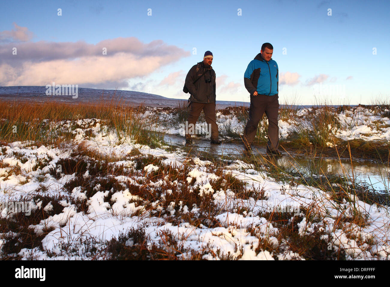 After light snowfall, walkers cross moorlands at dusk on the Pennine ...