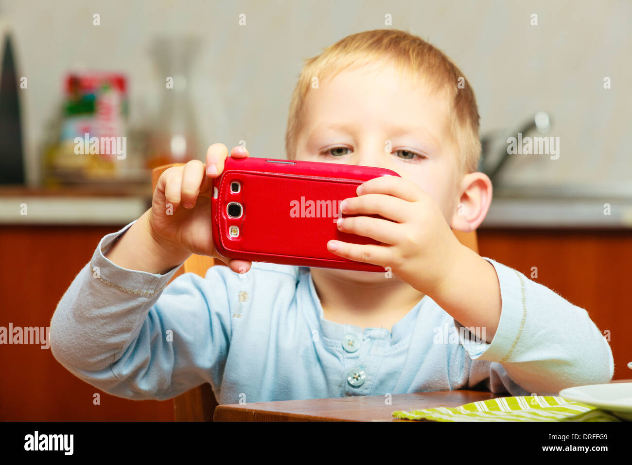 Happy childhood. Blond boy kid child playing with mobile phone at the ...