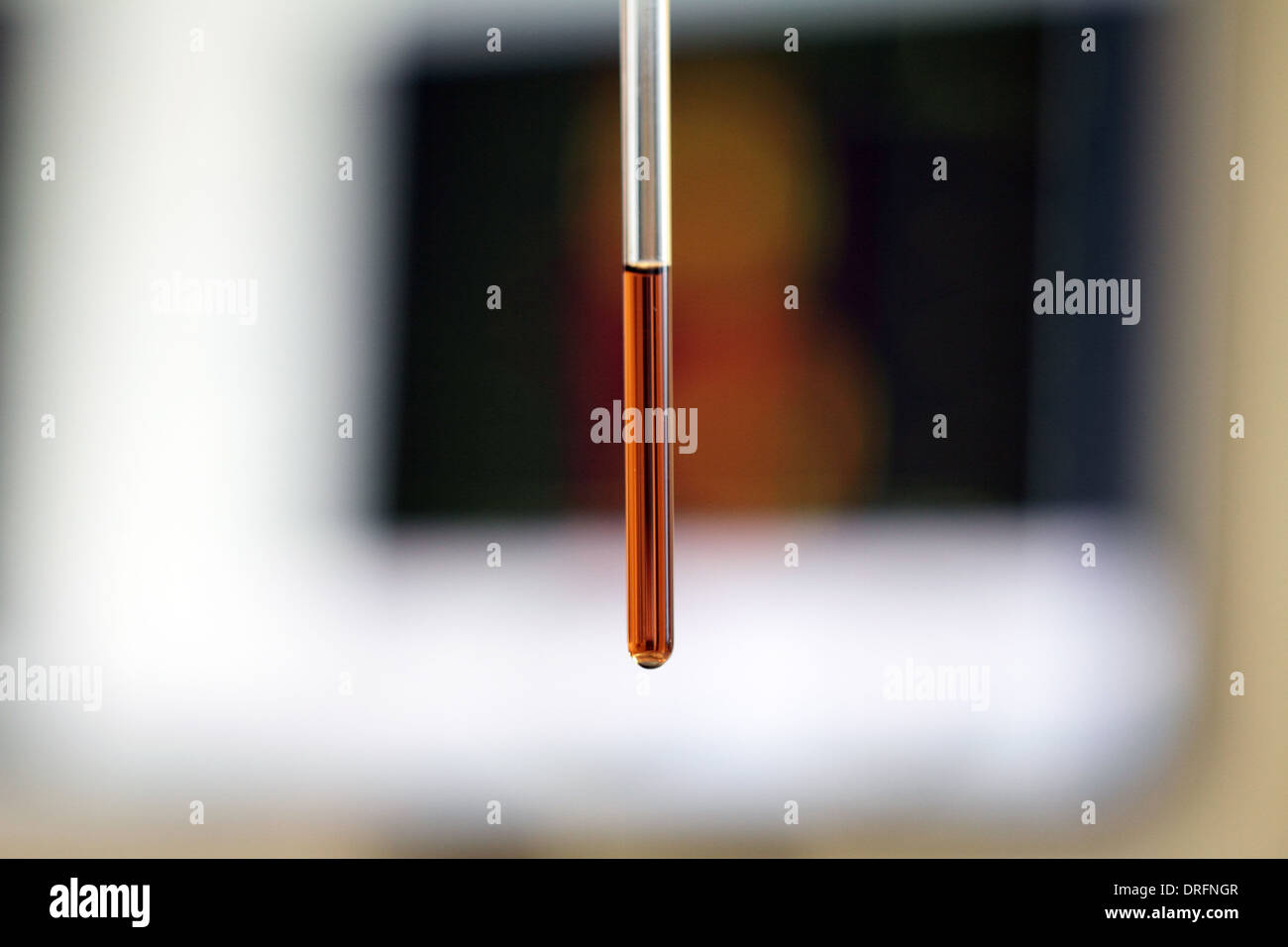 small glass tube with liquid and a monitor image in the background ...