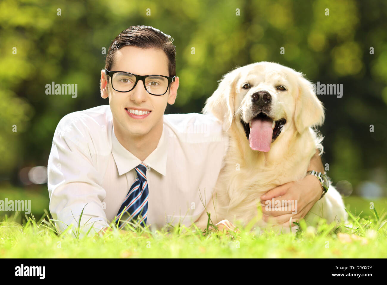 Guy lying on a grass and hugging his labrador retriever dog in a park ...