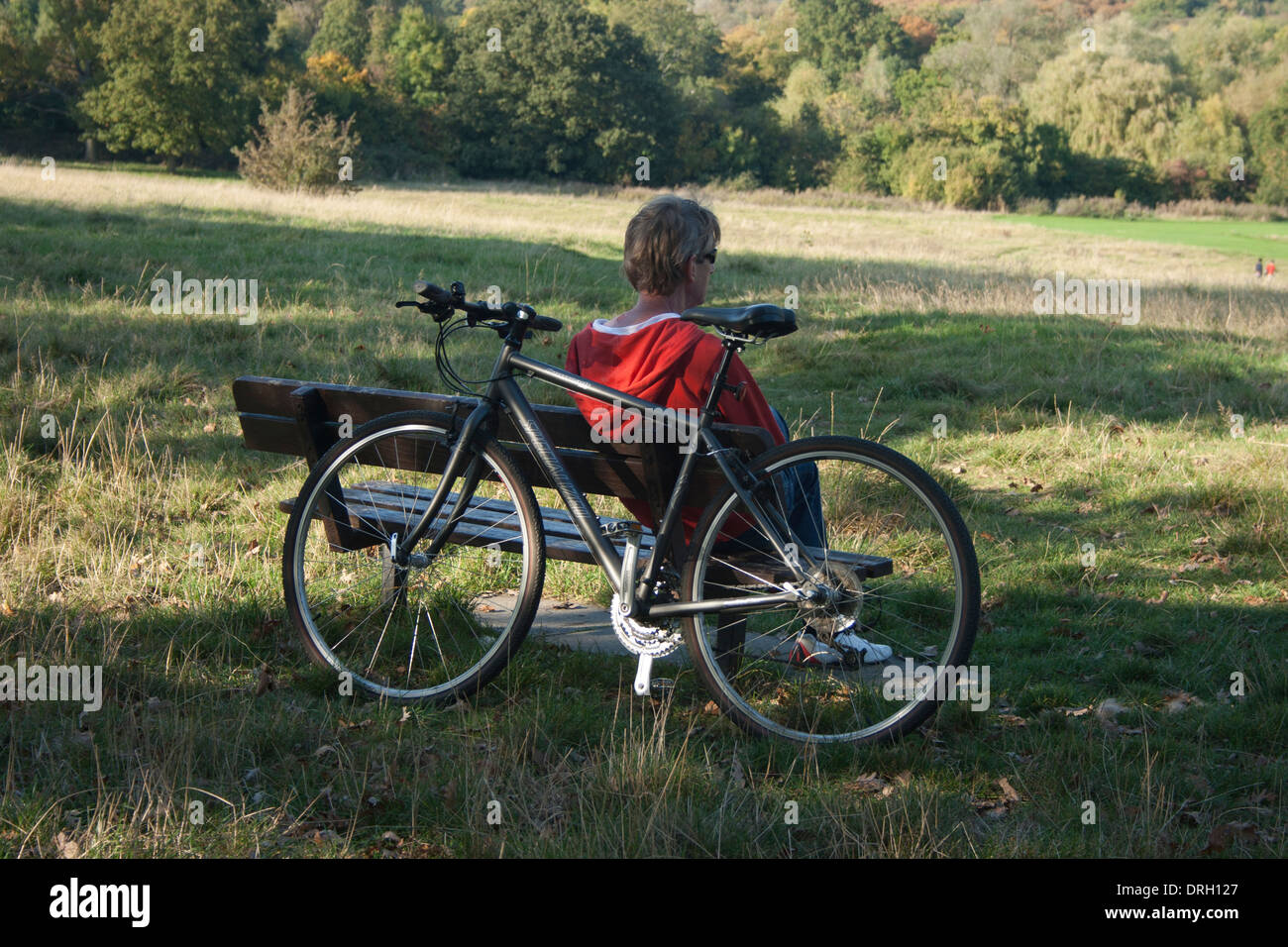 Cyclist on bench at Hampstead Heath with bike leaning aganist the bench ...