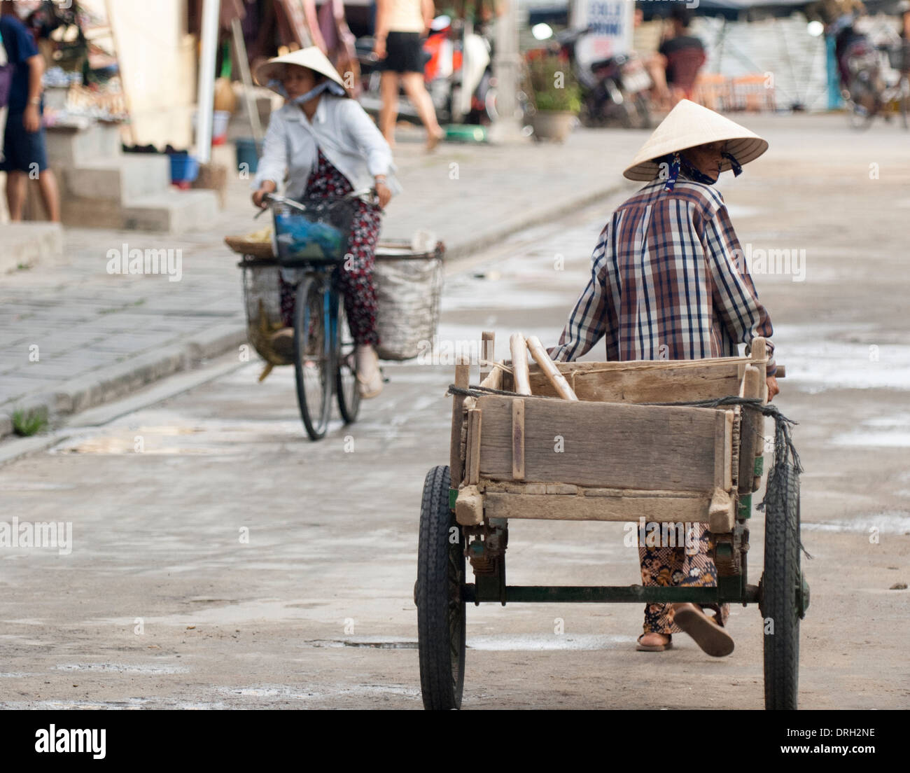 Man pulling cart and cyclist with conical hats, Hoi An, Vietnam Stock ...