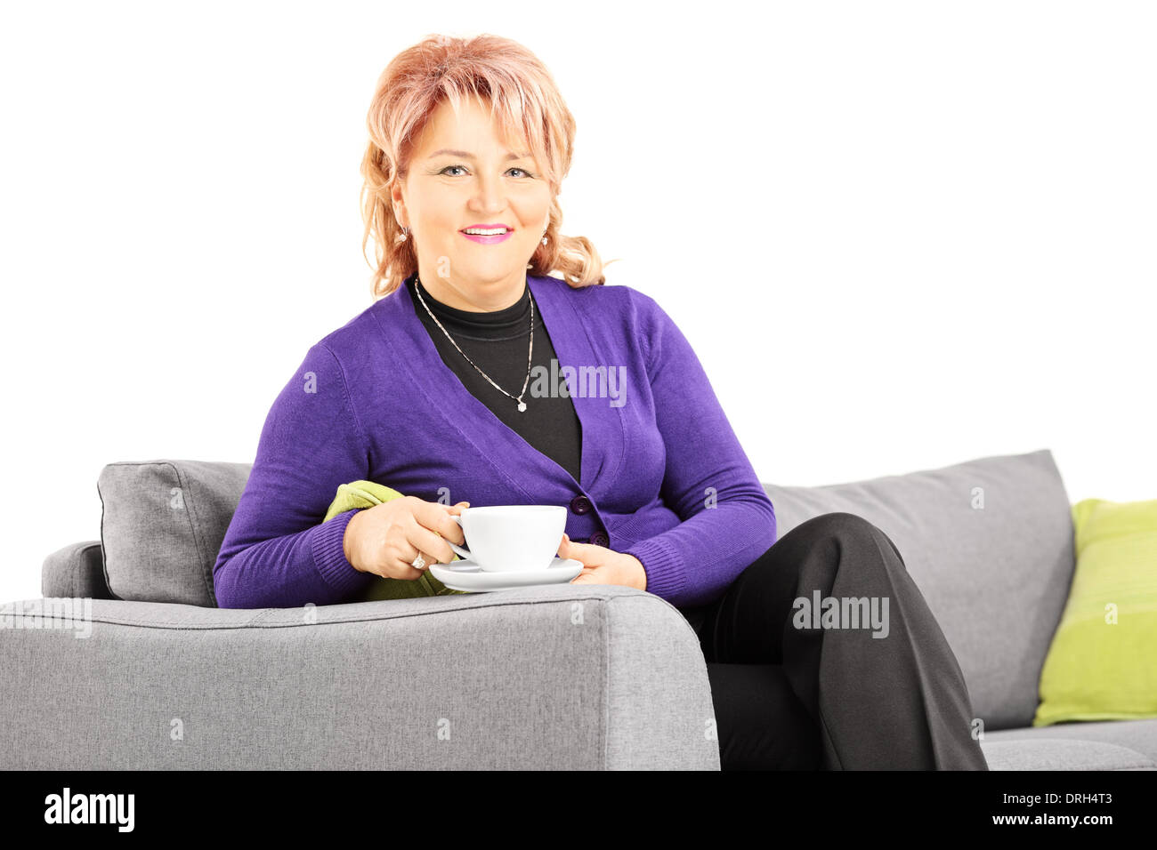 Mature lady seated on a sofa holding a cup of coffee and looking at ...