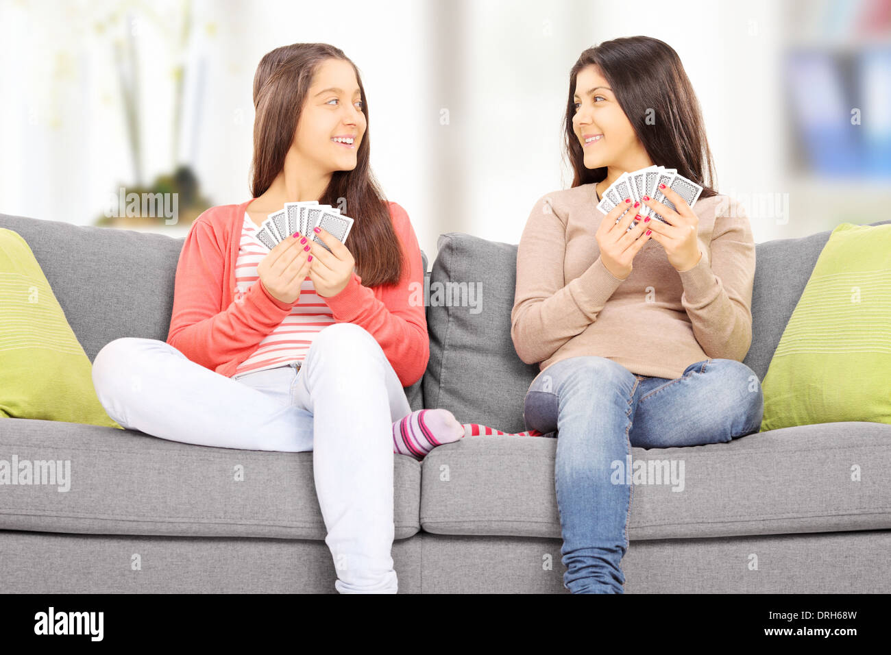 Two teenage girls sitting on sofa playing cards, at home Stock Photo ...