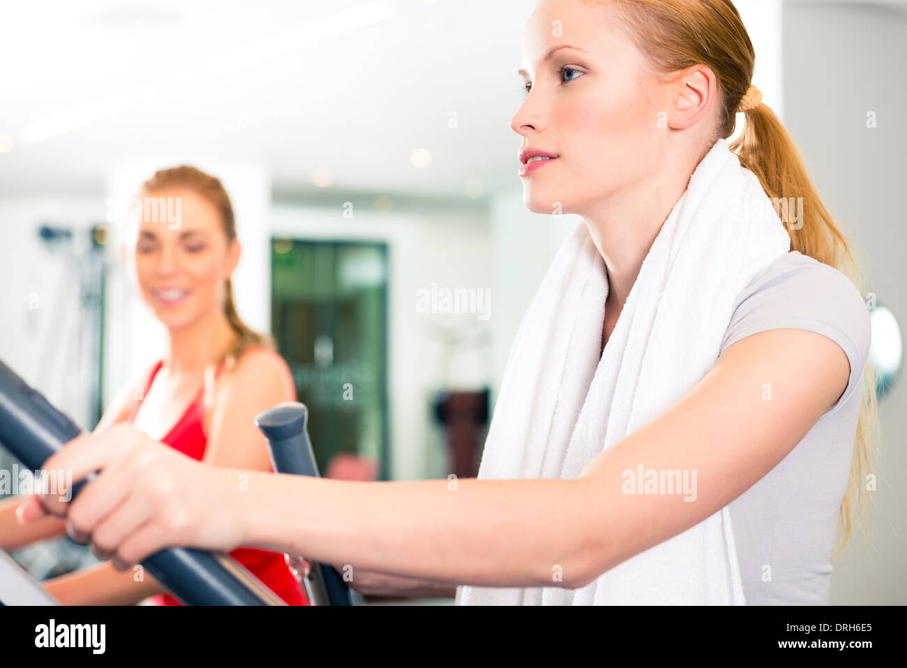 Two young women training on cardio or endurance machine in gym sport ...