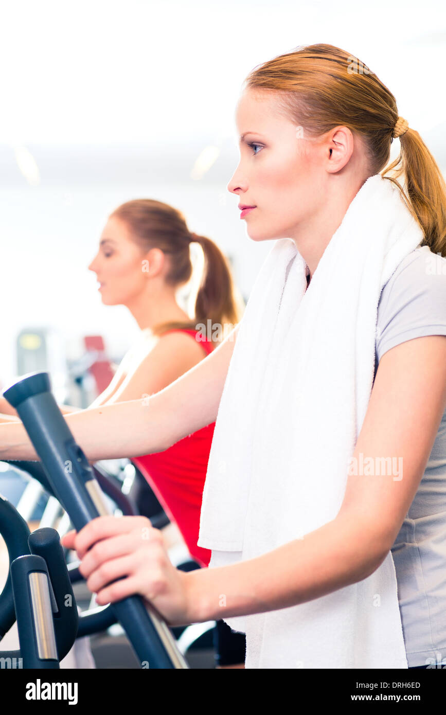 Two young women training on cardio or endurance machine in gym sport ...