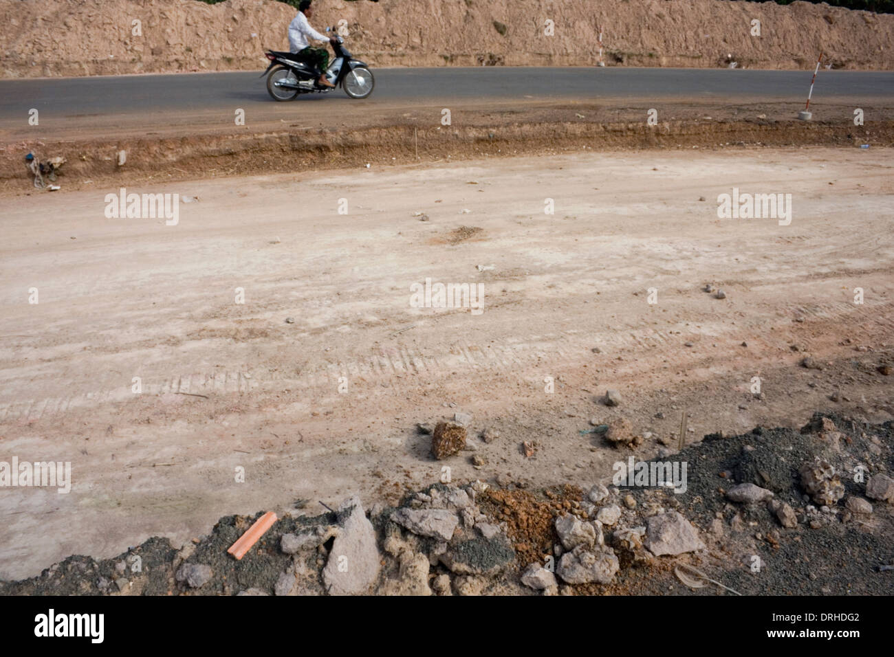 A man riding a motorcycle is passing a new road construction site in ...