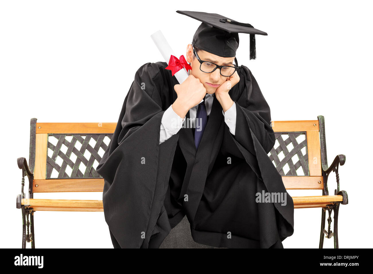 Worried student in graduation gown seated on bench holding diploma ...