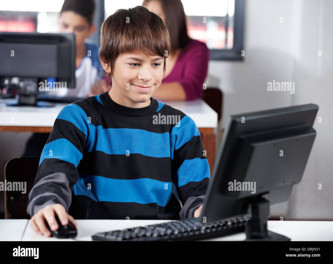Boy Smiling While Using Computer In Classroom Stock Photo - Alamy