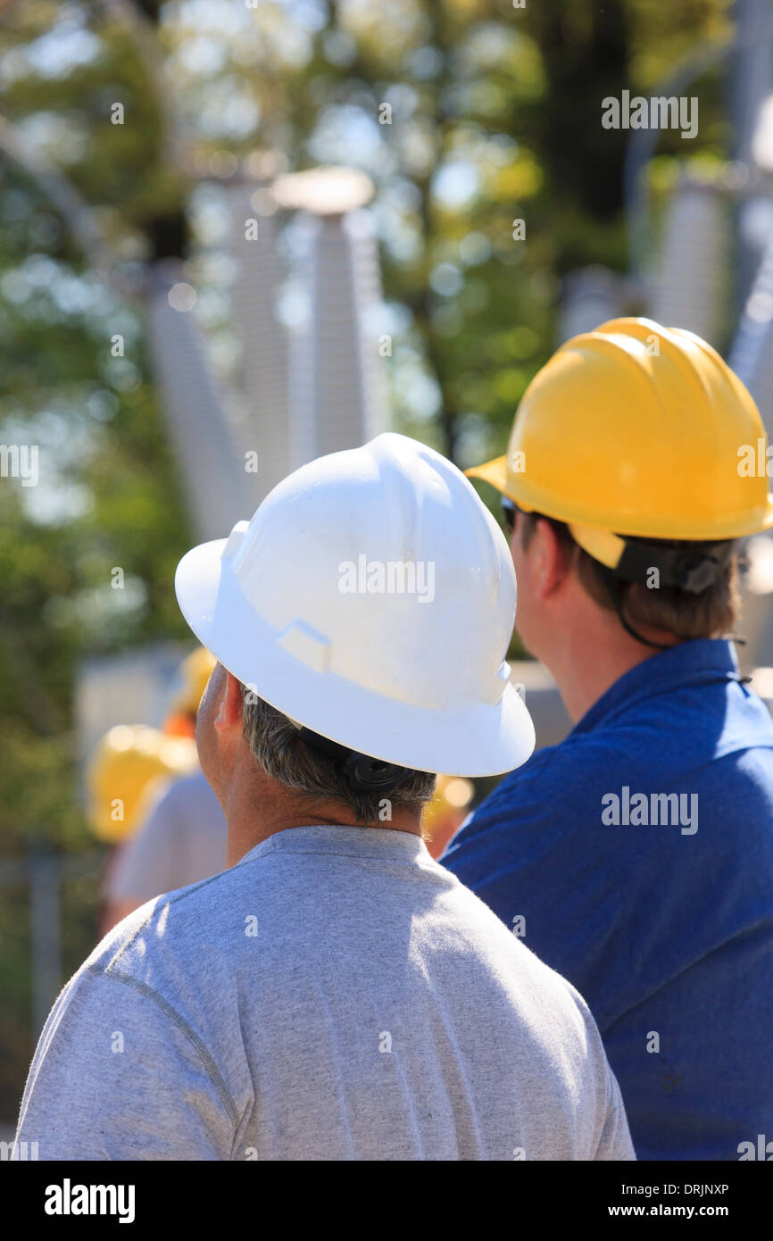 Power engineers looking at high voltage power distribution station ...