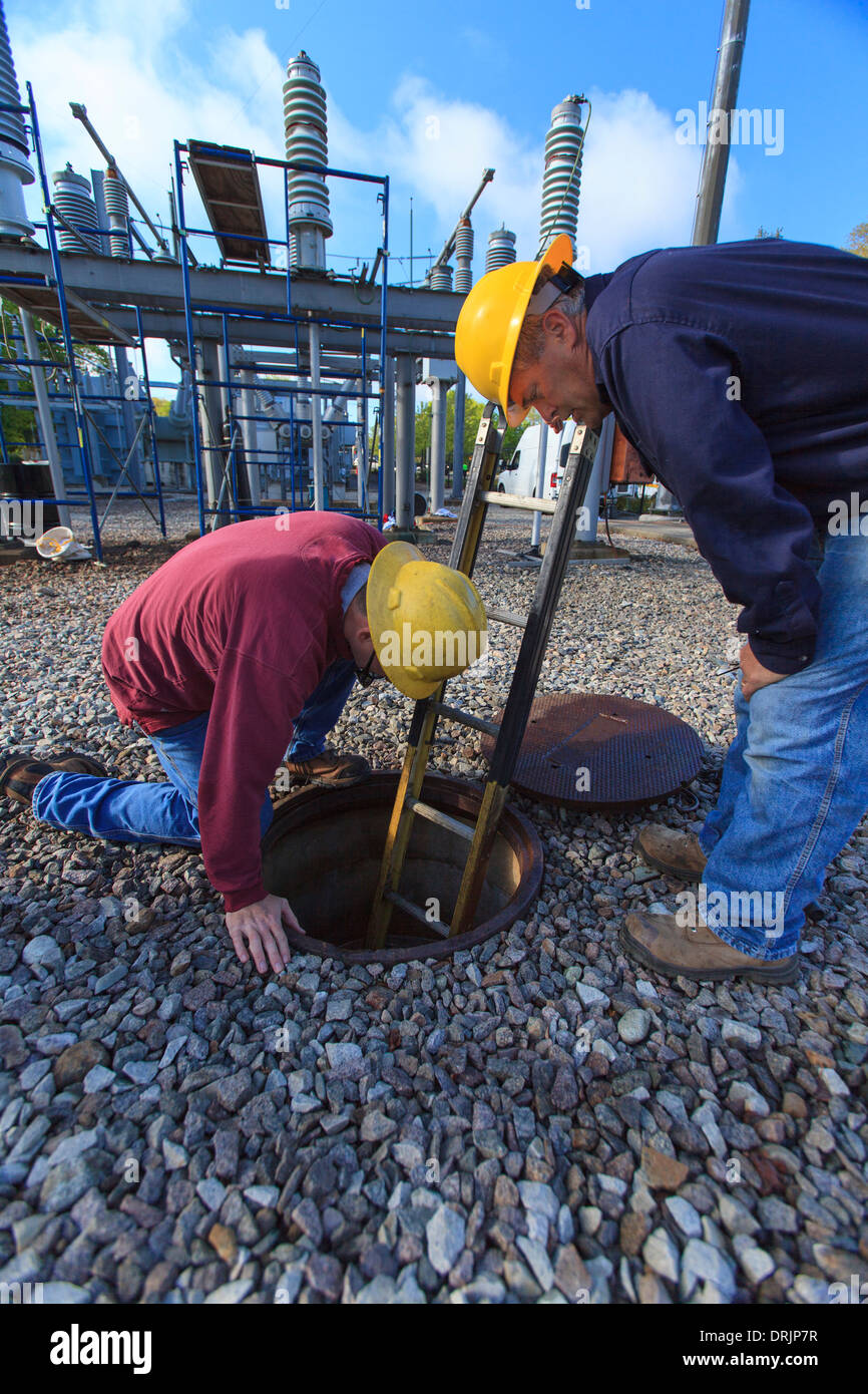 Power engineers placing ladder inside manhole at high voltage power ...