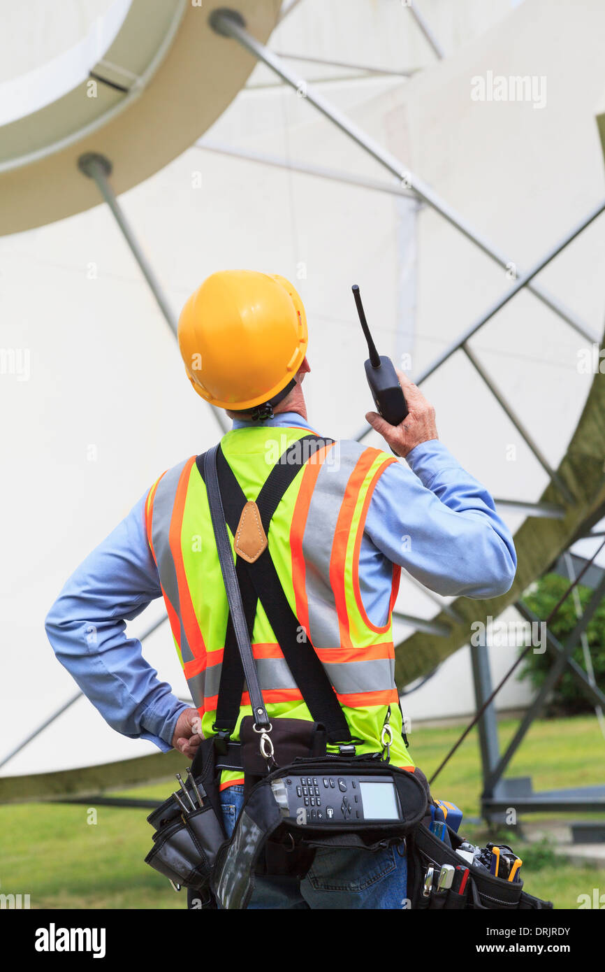 Communications engineer using walkie-talkie at satellite antenna ...