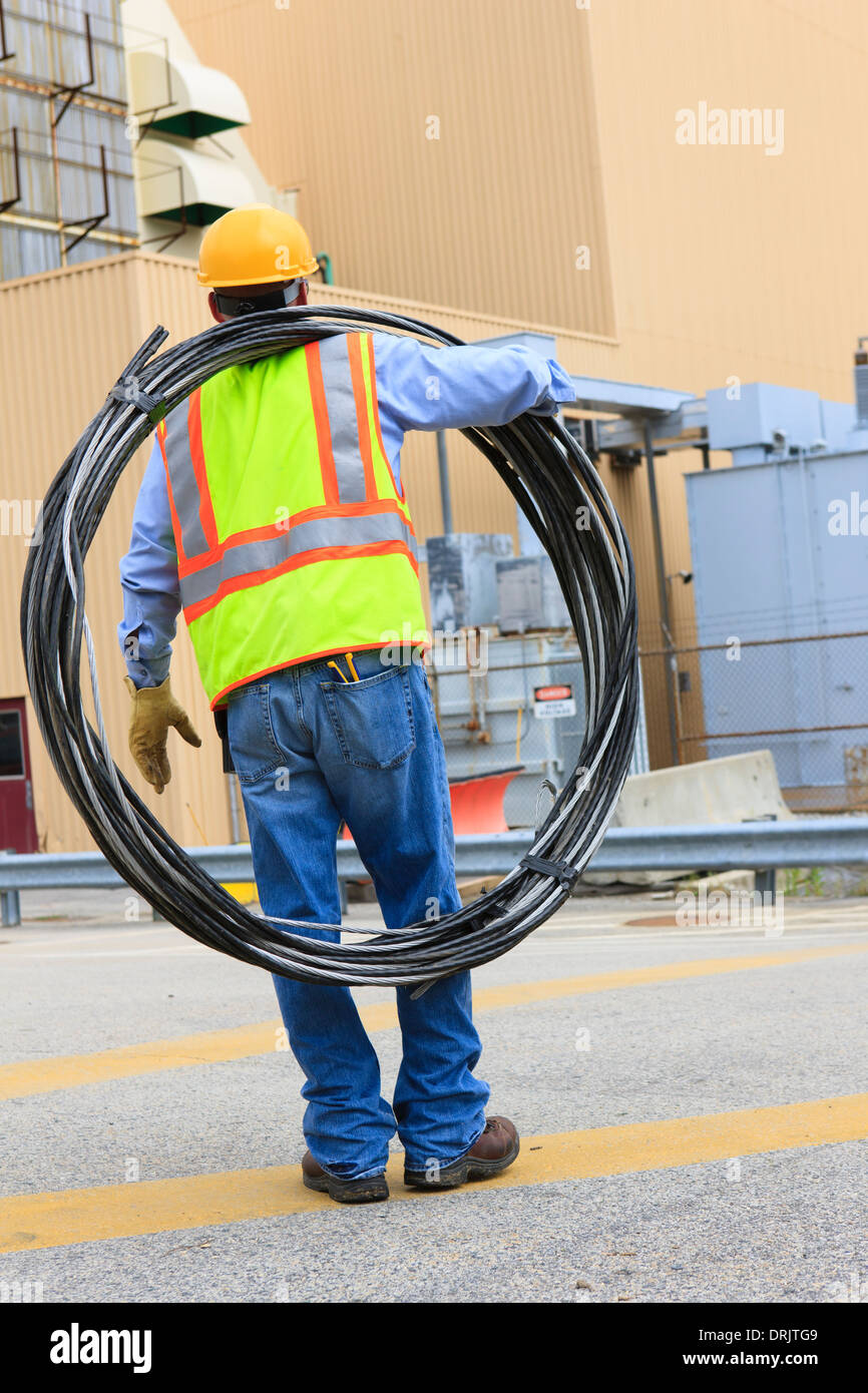 Engineer at electric power plant carrying coil of wire at storage area ...