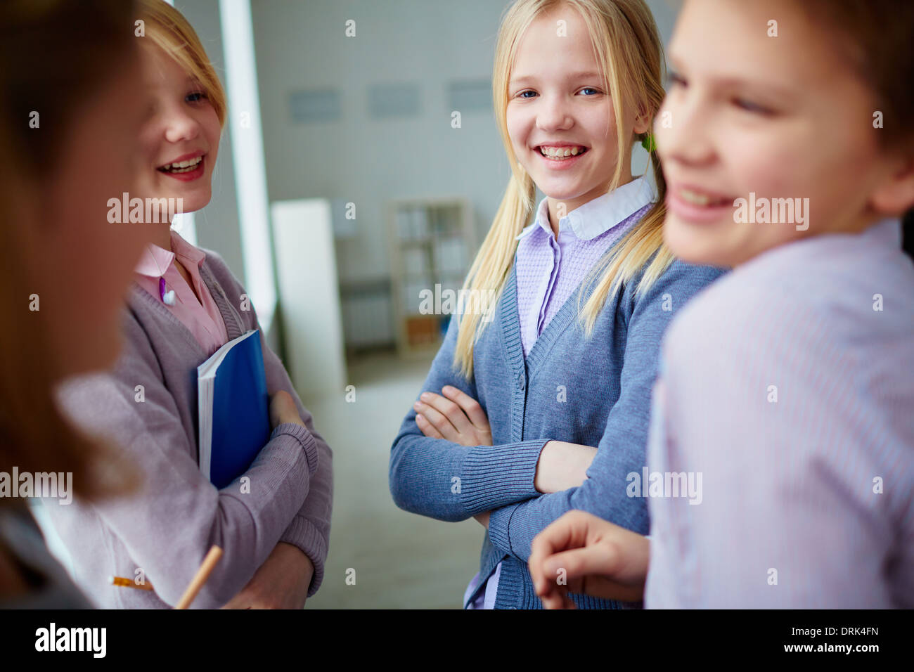 Portrait of three happy schoolgirls and schoolboy talking during school ...