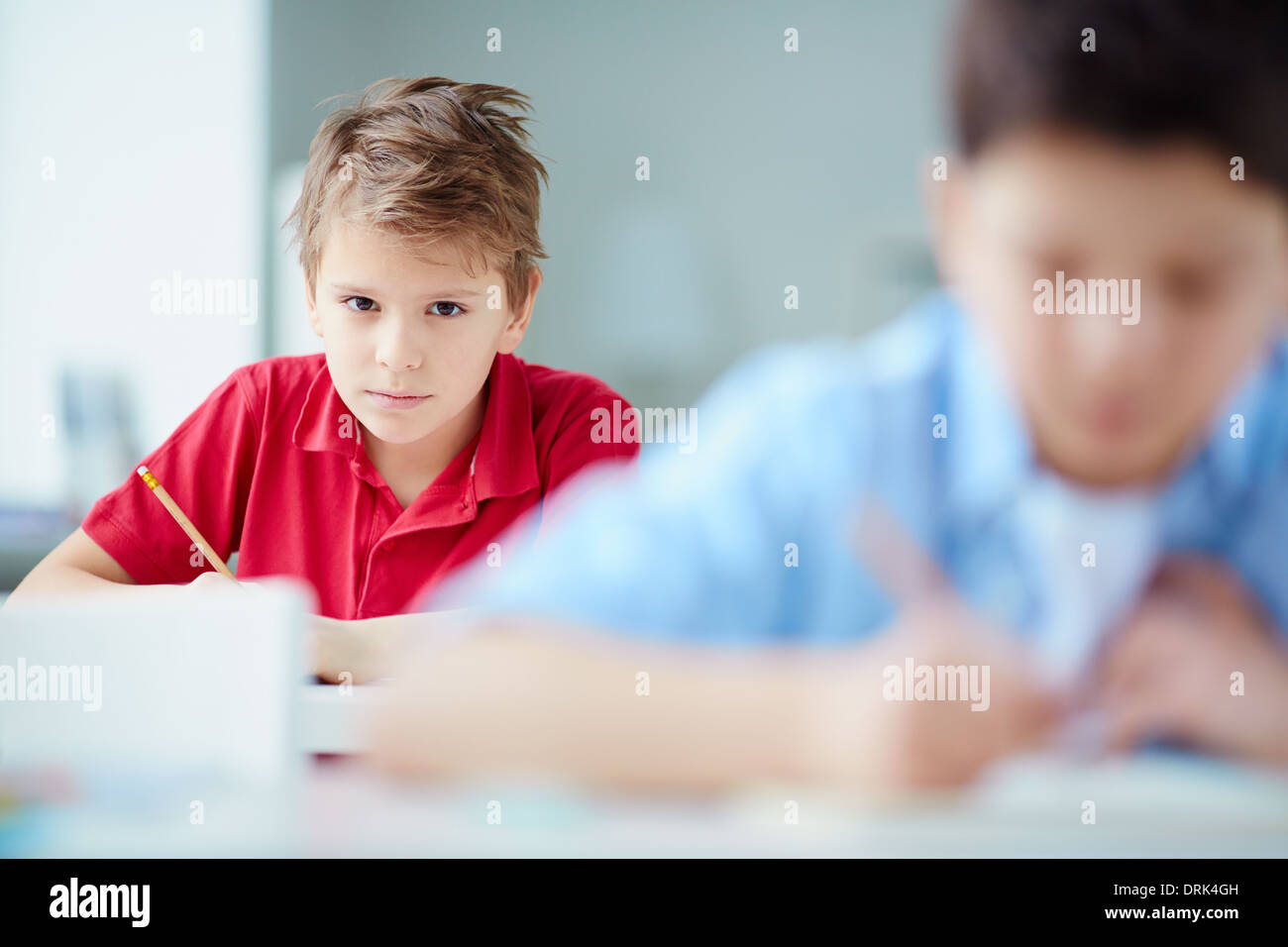 Portrait of serious schoolboy looking at camera while drawing at lesson ...