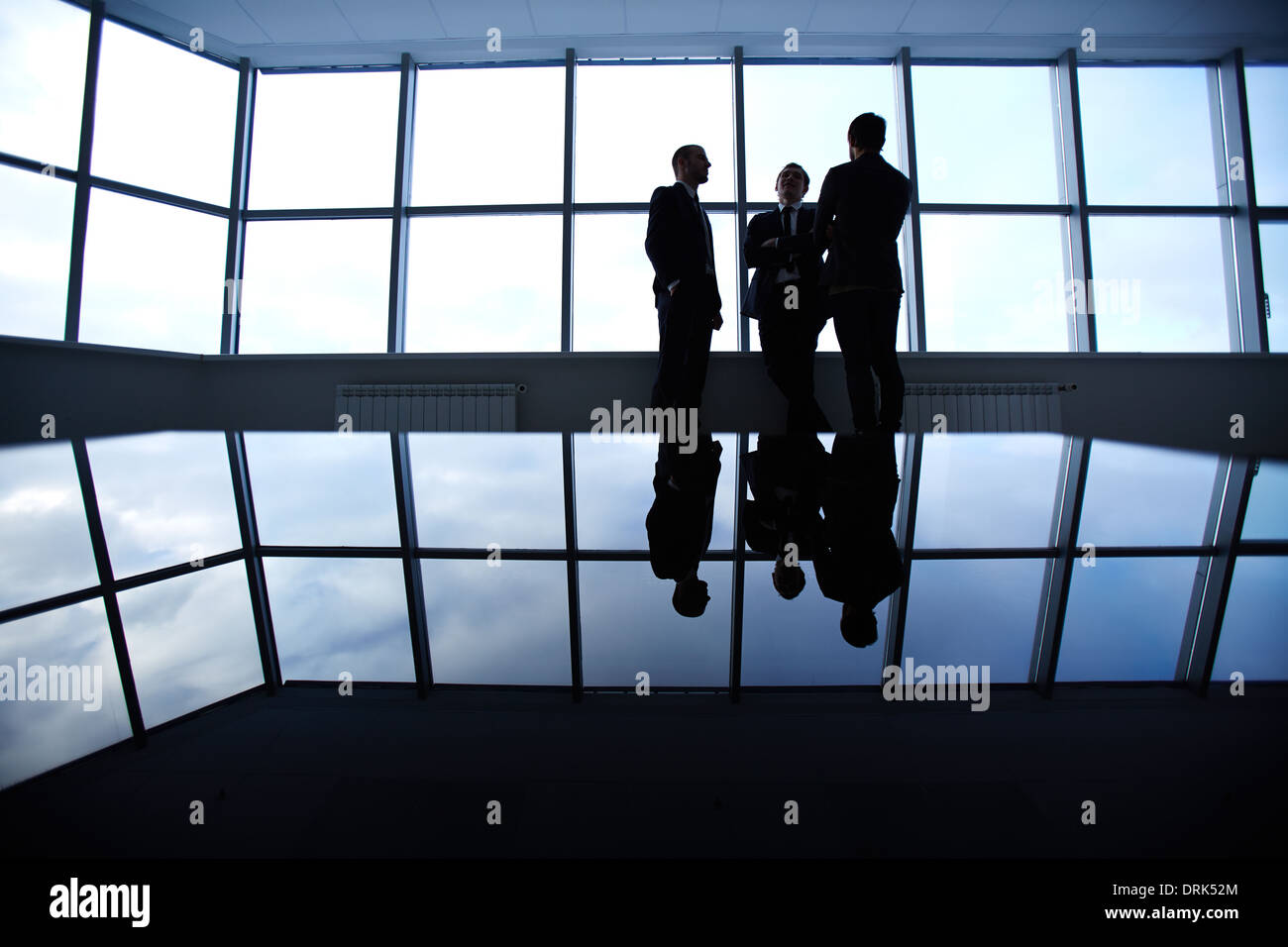 Group of colleagues standing against window in office and speaking ...