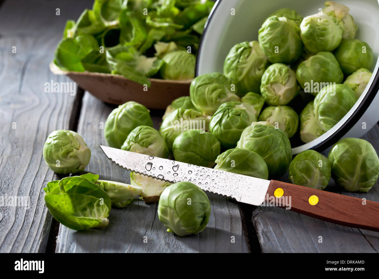 Bowl of Brussels sprouts, plate with peels and kitchen knife on grey ...