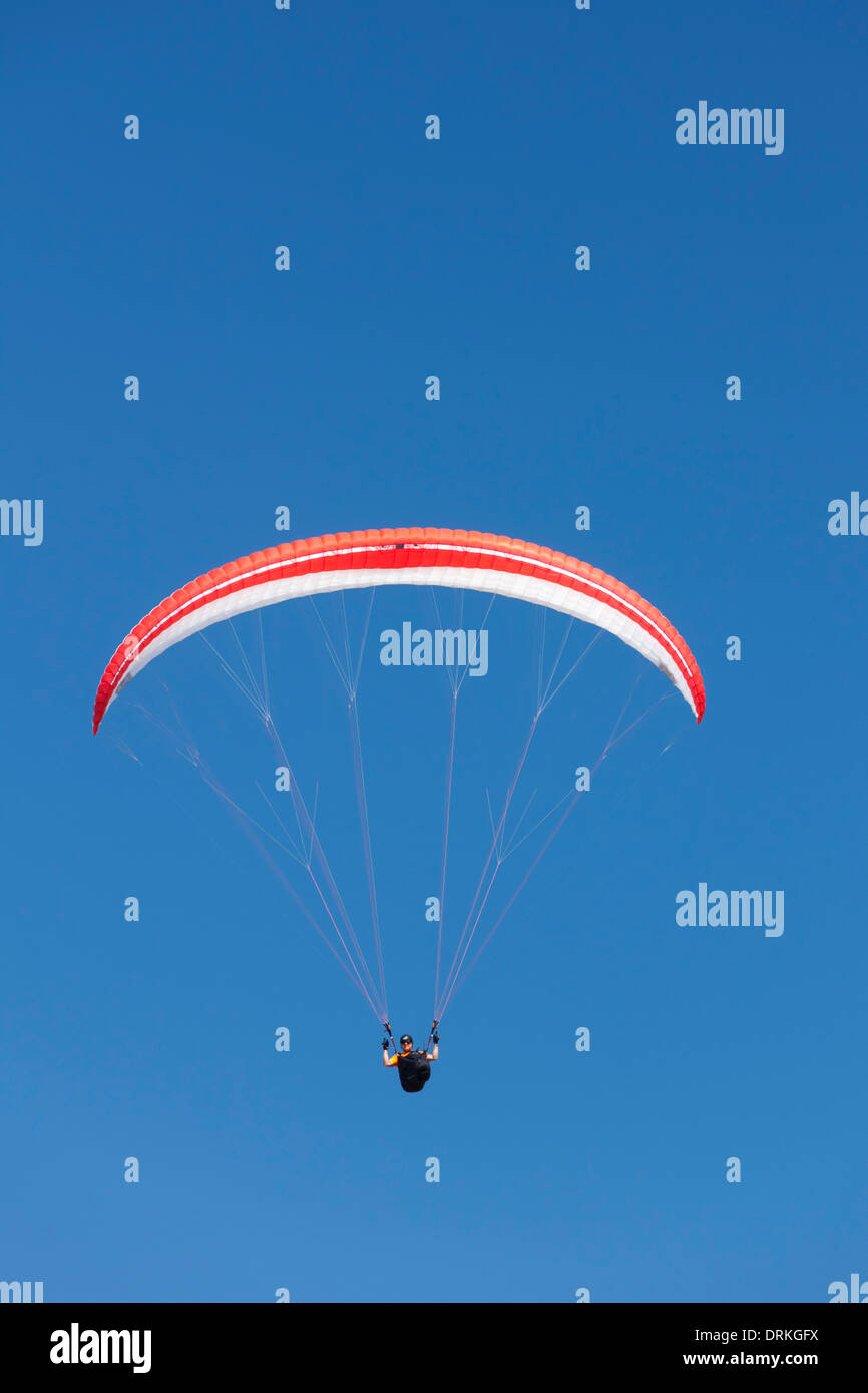 Paraglider in flight with colourful wing / canopy against blue sky ...