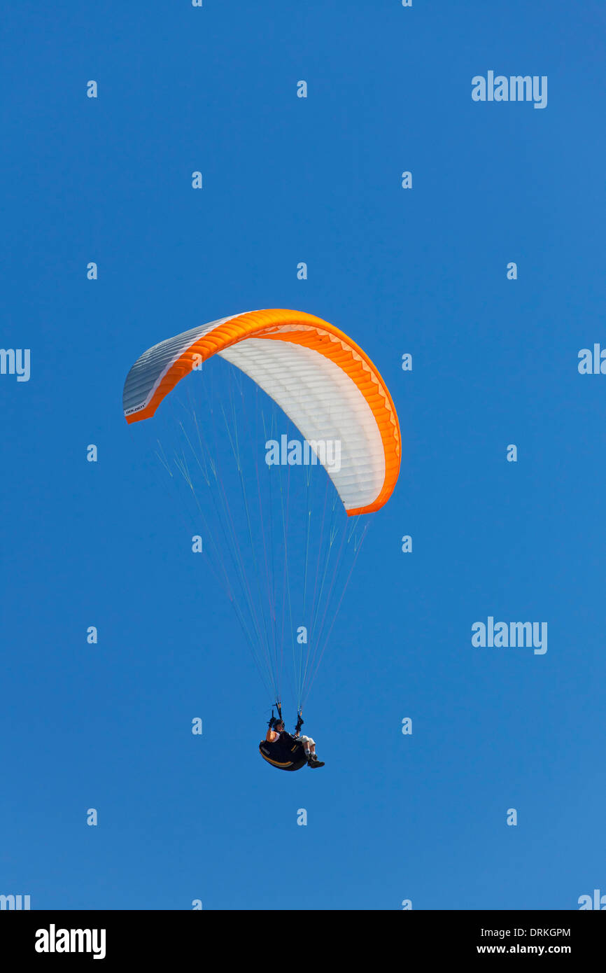 Paraglider in flight with colourful wing / canopy against blue sky ...