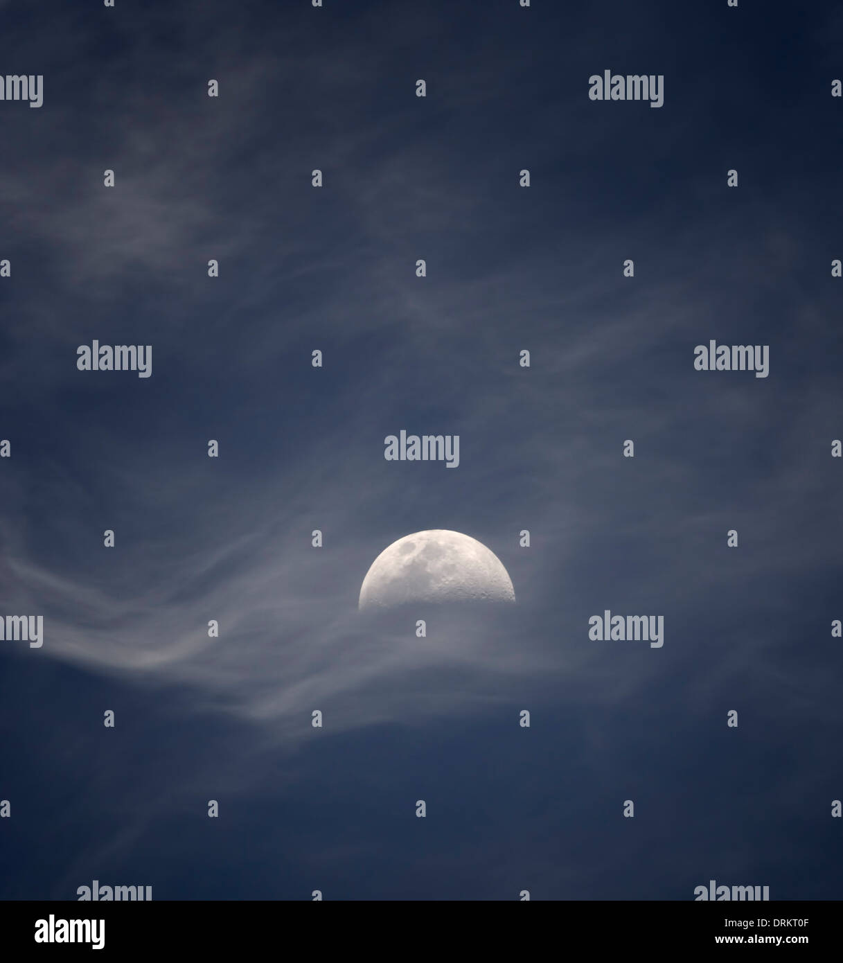 A half moon floats in a grouping of Cirrus clouds in the evening sky ...