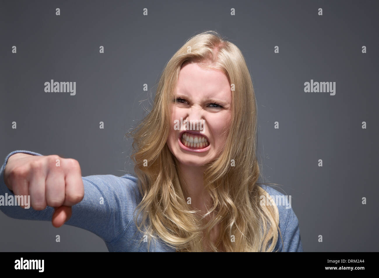 Portrait of furious young woman with outstretched fist and bared teeth ...