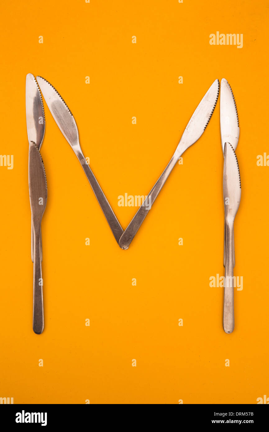 Letter "M" formed of knives at yellow background, studio shot Stock ...