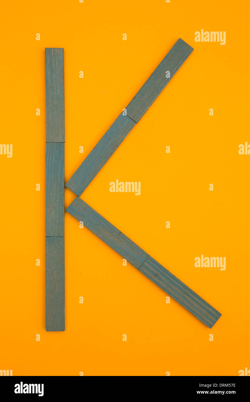 Letter "K" formed of blue building bricks at yellow background, studio ...