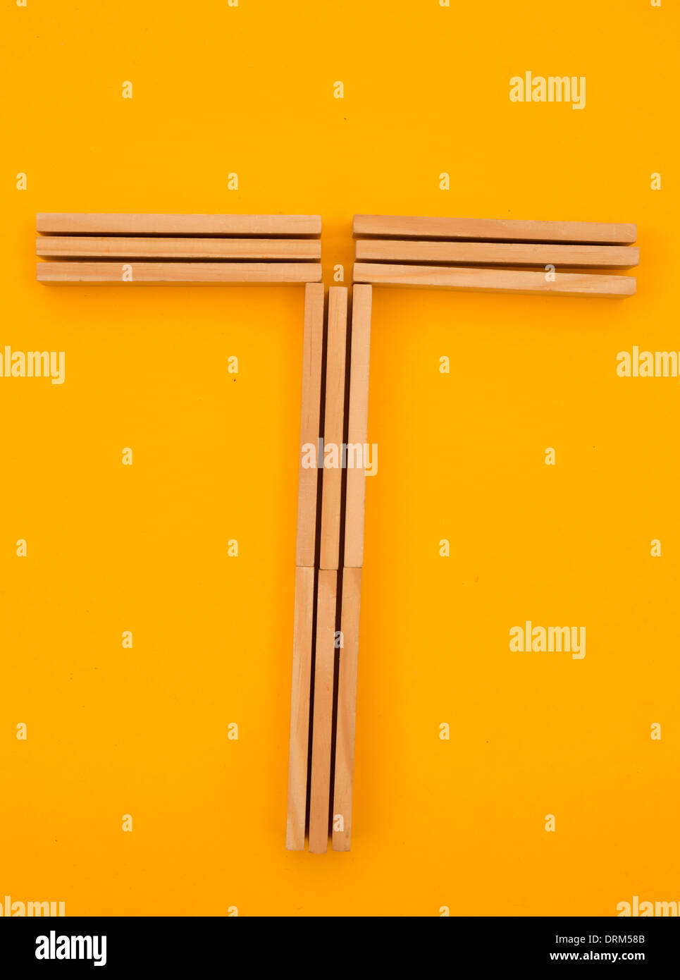 Letter "T" formed of building bricks at yellow background, studio shot ...