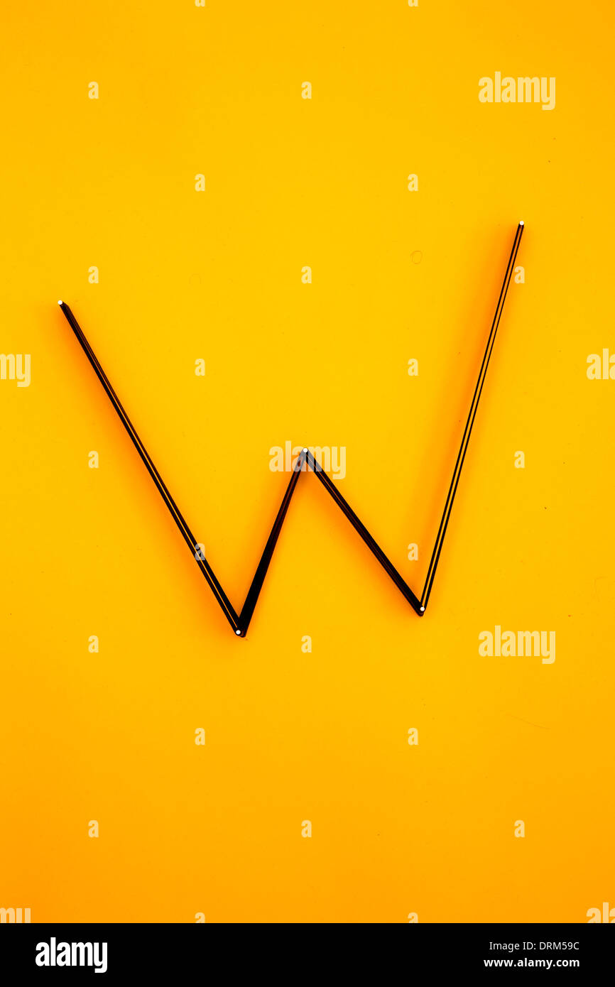 Letter "W" formed of nails and threads at yellow background, studio ...