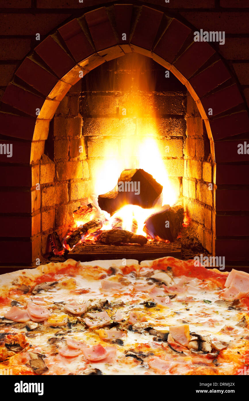 italian pizza with ham and mushrooms and open fire in wood burning ...