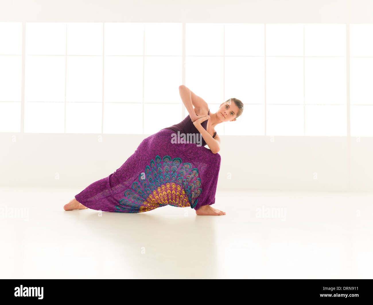 young girl in twisted yoga posture, dressed with pants skirt colorful ...