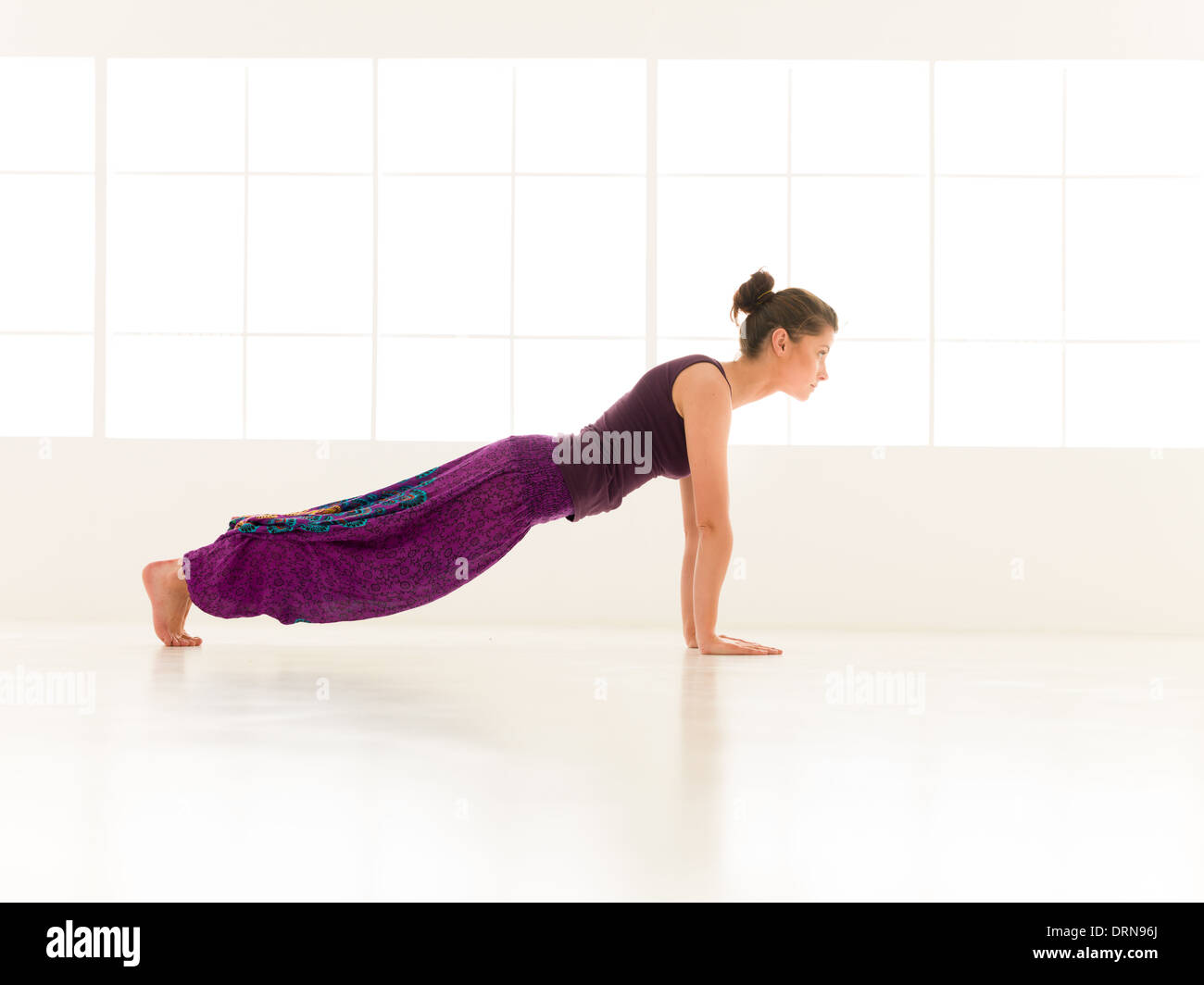 full side view of young woman demonstrating balancing yoga pose ...