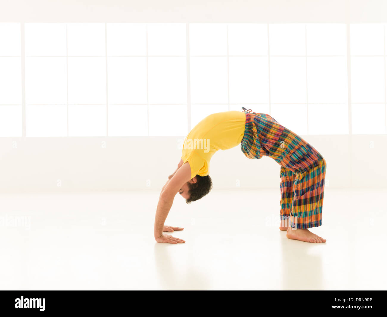 Colorful dressed male repeating Dhanurasana yoga exercises in a white ...