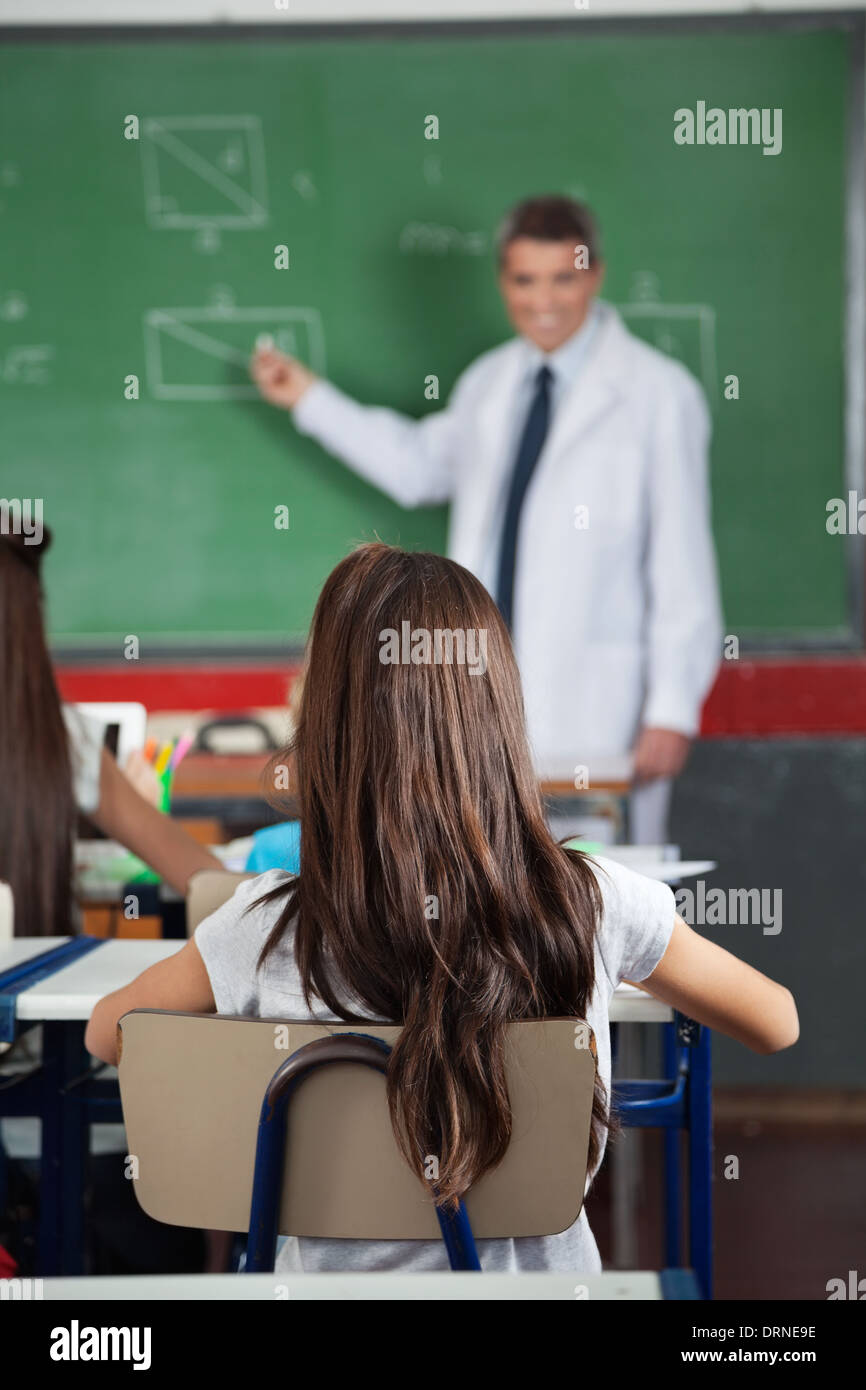 Girl Sitting At Desk With Teacher Teaching In Background Stock Photo ...