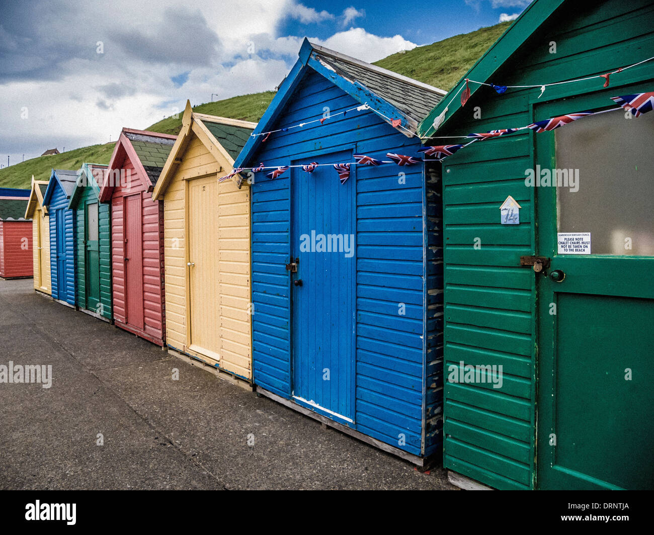 Colourful beach huts decorated with bunting at the base of West Cliff ...