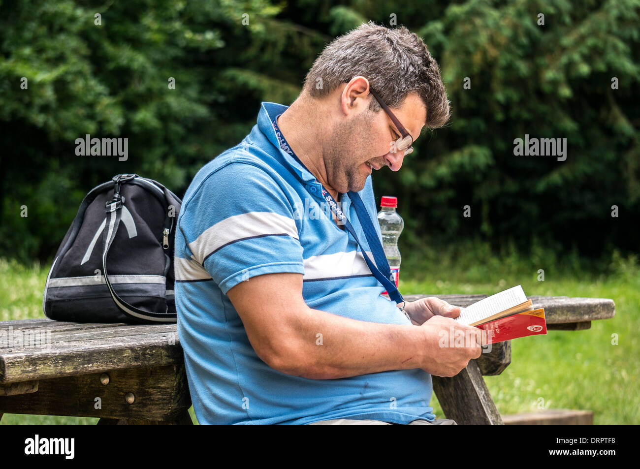 A man sitting down, relaxing outside in the sunshine, reading a book at ...