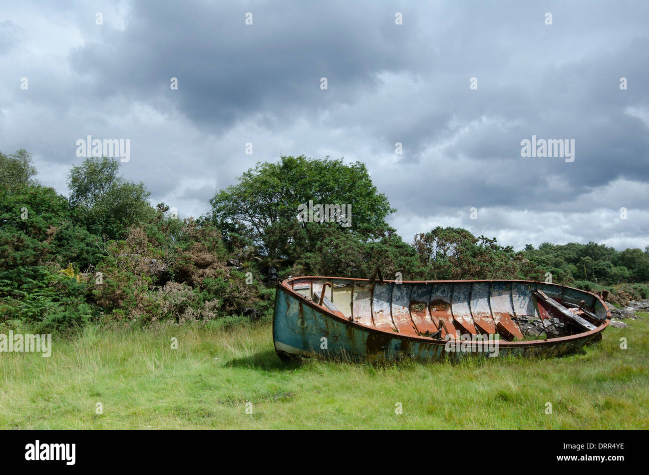 The hull of a old metal boat rotting and rusting in a field in the sun ...