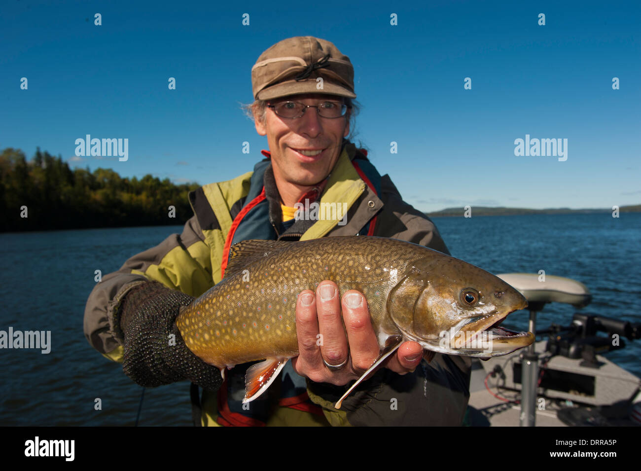 Fisherman holding a large summer brook trout he caught from his boat in ...