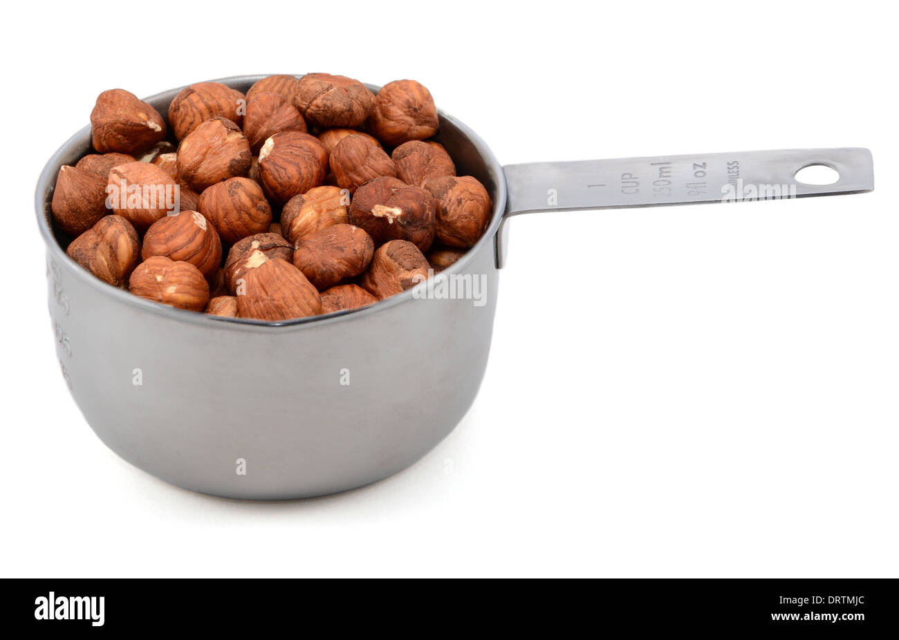Whole hazelnuts in a metal cup measure, isolated on a white background ...