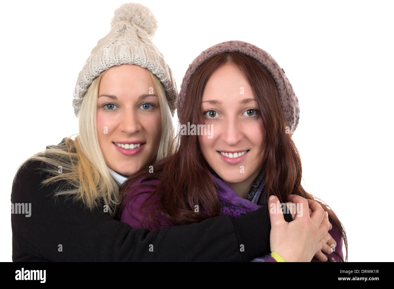 Two young women in winter clothing hug each other, isolated on a white ...